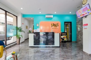 Uma área de recepção de hotel com design moderno, apresentando um balcão de atendimento, um relógio e uma tela de televisão.
