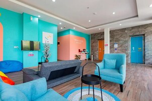 Um hall com paredes verde-água e pêssego, um sofá cinzento, uma poltrona azul, uma mesa pequena e um balcão de recepção.