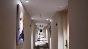 Corredor de hotel com piso xadrez, paredes brancas e portas à direita.