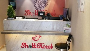 Bancada de recepção de hotel com tampos de mármore, uma planta em vaso e uma placa com a inscrição "Shobol Hotel".