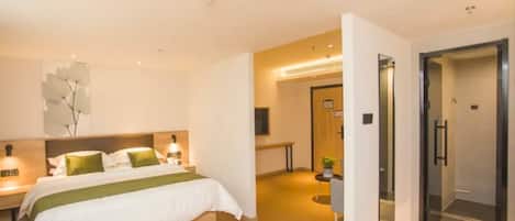 Quarto de hotel moderno com uma cama grande, mesas de cabeceira, uma pequena escrivaninha e área de chuveiro.