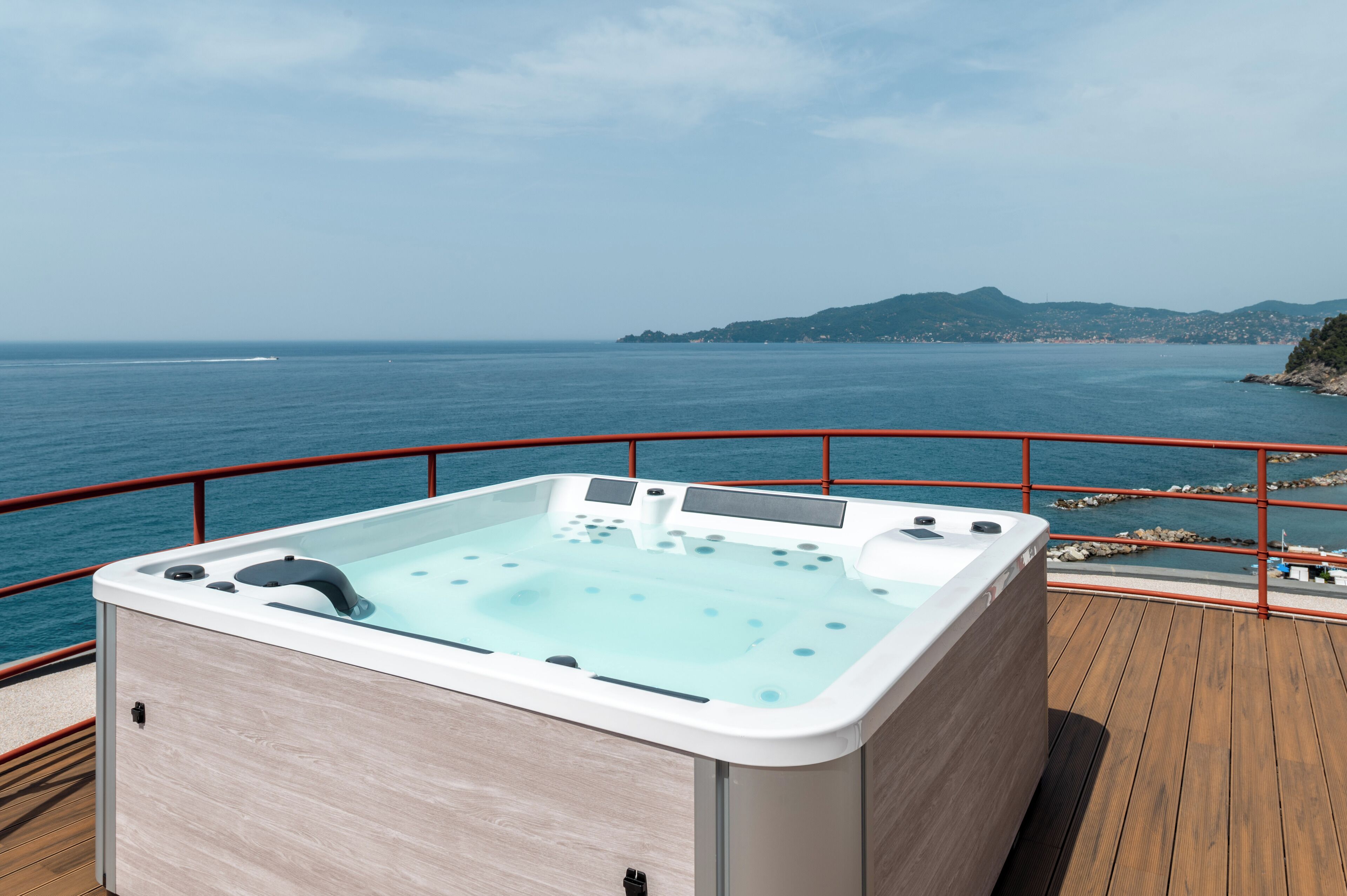Uma banheira de hidromassagem em um deck com vista para o mar e uma ilha distante.