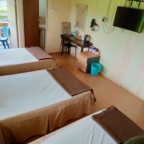 Quarto de hotel com duas camas, uma escrivaninha, uma cadeira, uma televisão e um cesto de lixo.