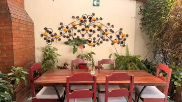 Uma mesa de madeira com cadeiras vermelhas, um objeto decorativo na parede e plantas em vasos.