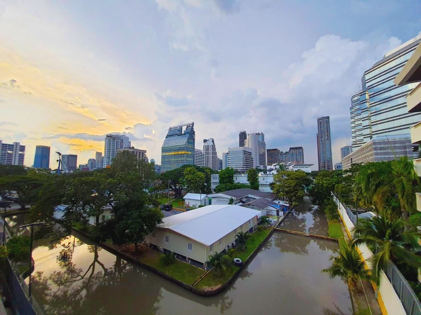 Paisagem urbana com edifícios modernos altos, um corpo de água e um edifício branco com telhado plano em primeiro plano.