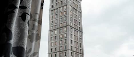 Vista de um edifício alto através de uma janela com cortinas florais.