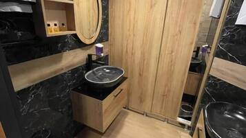 Uma cozinha compacta com bancada preta, armários de madeira e painel de fundo de mármore.