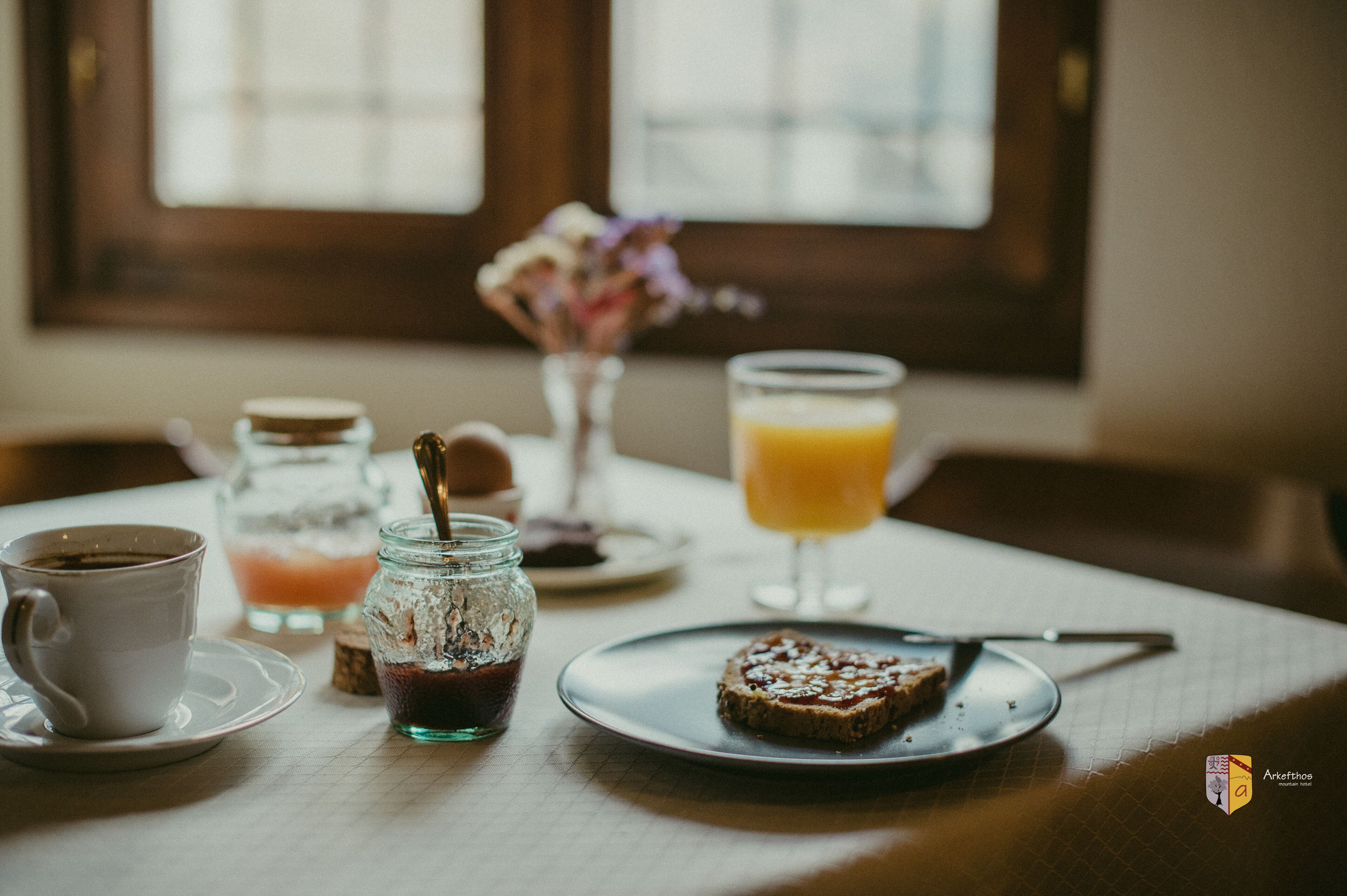 Uma mesa de café da manhã com uma xícara de café, um copo de suco de laranja, um pote de geleia e uma fatia de torrada.