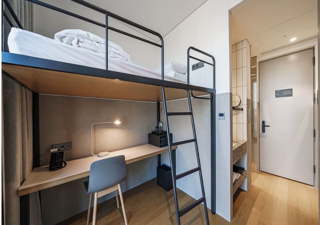 Uma cama beliche com escrivaninha e cadeira, uma escada, um telefone e uma porta com um aviso.
