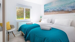 Quarto com duas camas, janela com vista para vegetação e pintura de ondas na parede.