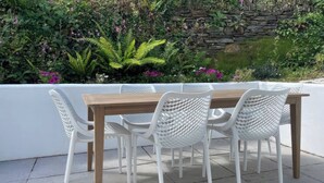 Uma mesa de madeira com cadeiras brancas em ambiente externo.