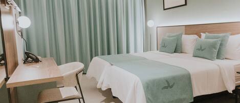 Quarto de hotel com uma cama, escrivaninha, cadeira, abajur e cortina.