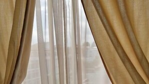 Quarto com cortinas leves, cama com roupa de cama listrada e vista para o exterior.
