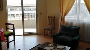 Sala de estar com sofá, poltrona e mesa de centro. Há uma porta de vidro deslizante que dá para uma varanda.