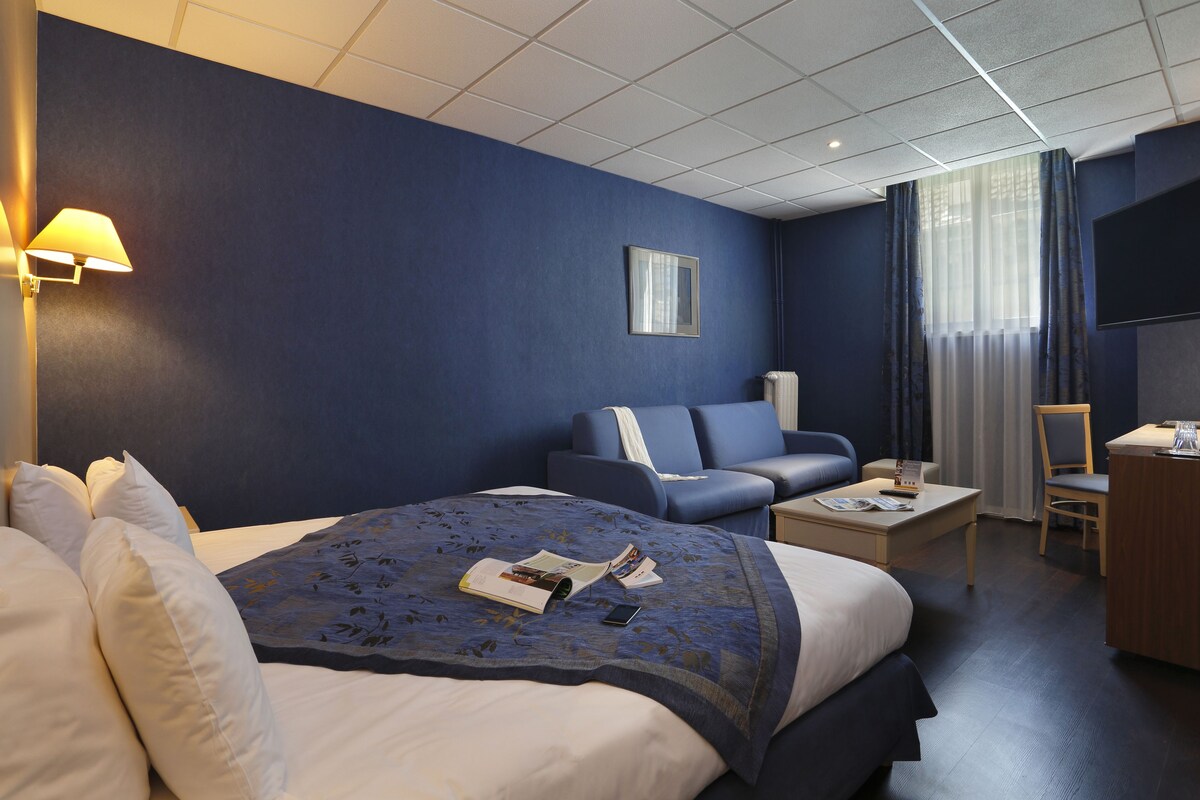 Quarto de hotel com uma cama grande, sofá, escrivaninha e televisão.