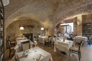 Um restaurante com paredes de pedra, mesas preparadas para refeições e garrafas de vinho em prateleiras.