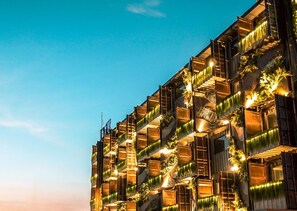 Um edifício com vários andares, varandas, escadas e iluminação externa.