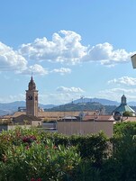 Vista de uma cidade com uma torre de igreja imponente e uma cadeia de montanhas ao fundo.
