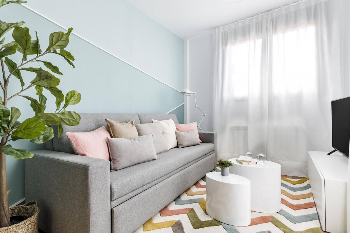 Uma sala de estar moderna com um sofá cinzento, mesas laterais brancas e uma planta grande.