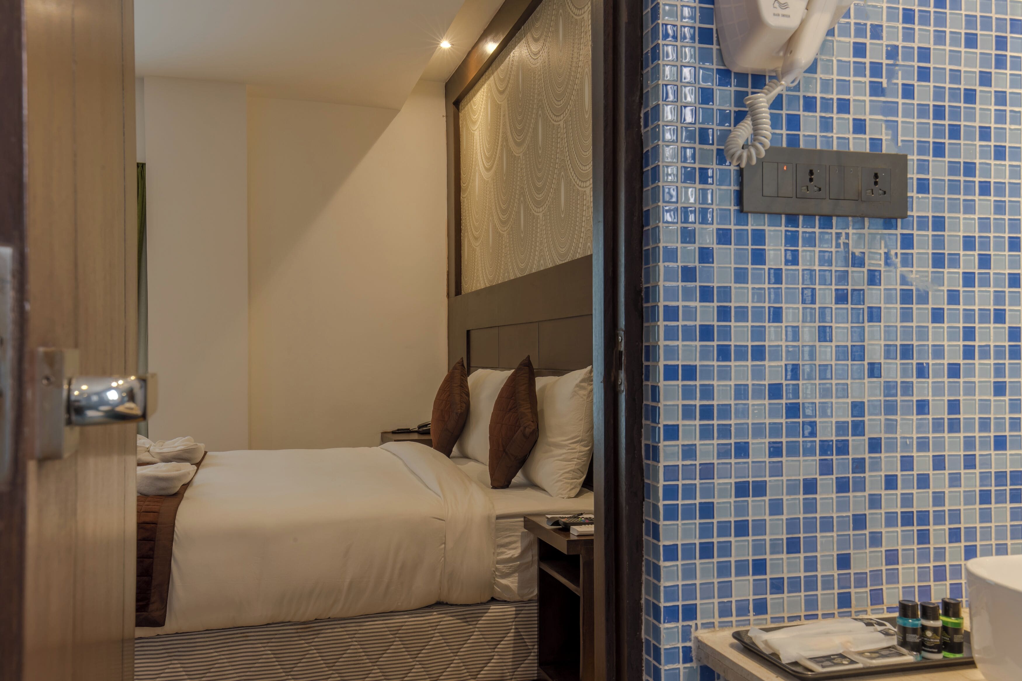 Quarto de hotel com cama, mesa de cabeceira, telefone e tomada na parede.