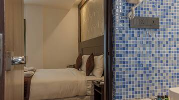 Quarto de hotel com cama, mesa de cabeceira, telefone e tomada na parede.