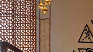 Uma escada com corrimão de madeira, parede decorativa com padrões geométricos e luminárias pendentes esféricas.