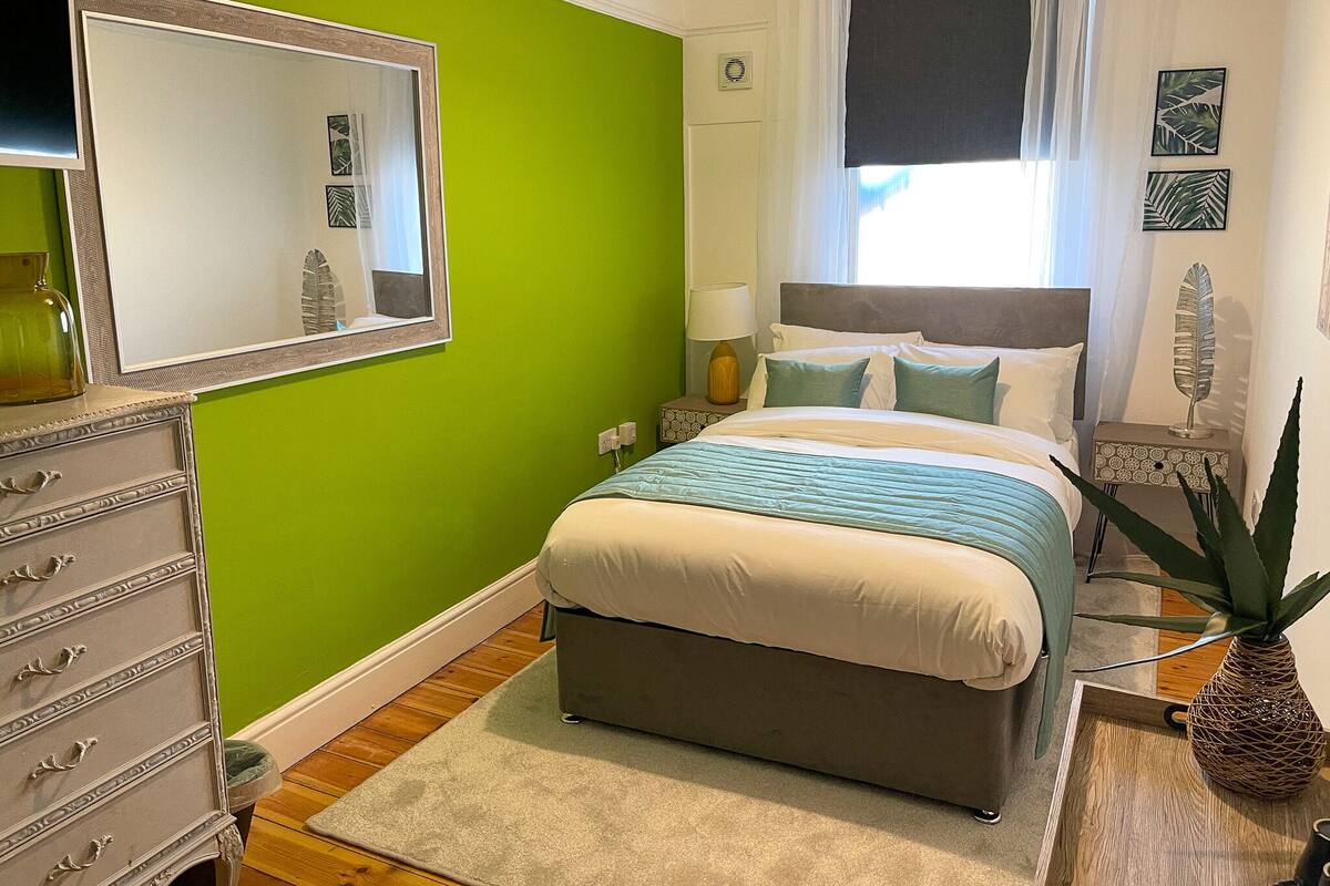 Quarto com cama, cómoda, mesa de cabeceira e um espelho grande.