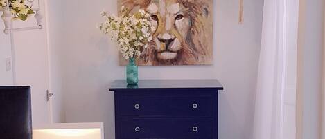 Um corredor com um aparador azul, um quadro com o rosto de um leão e uma planta pendente.