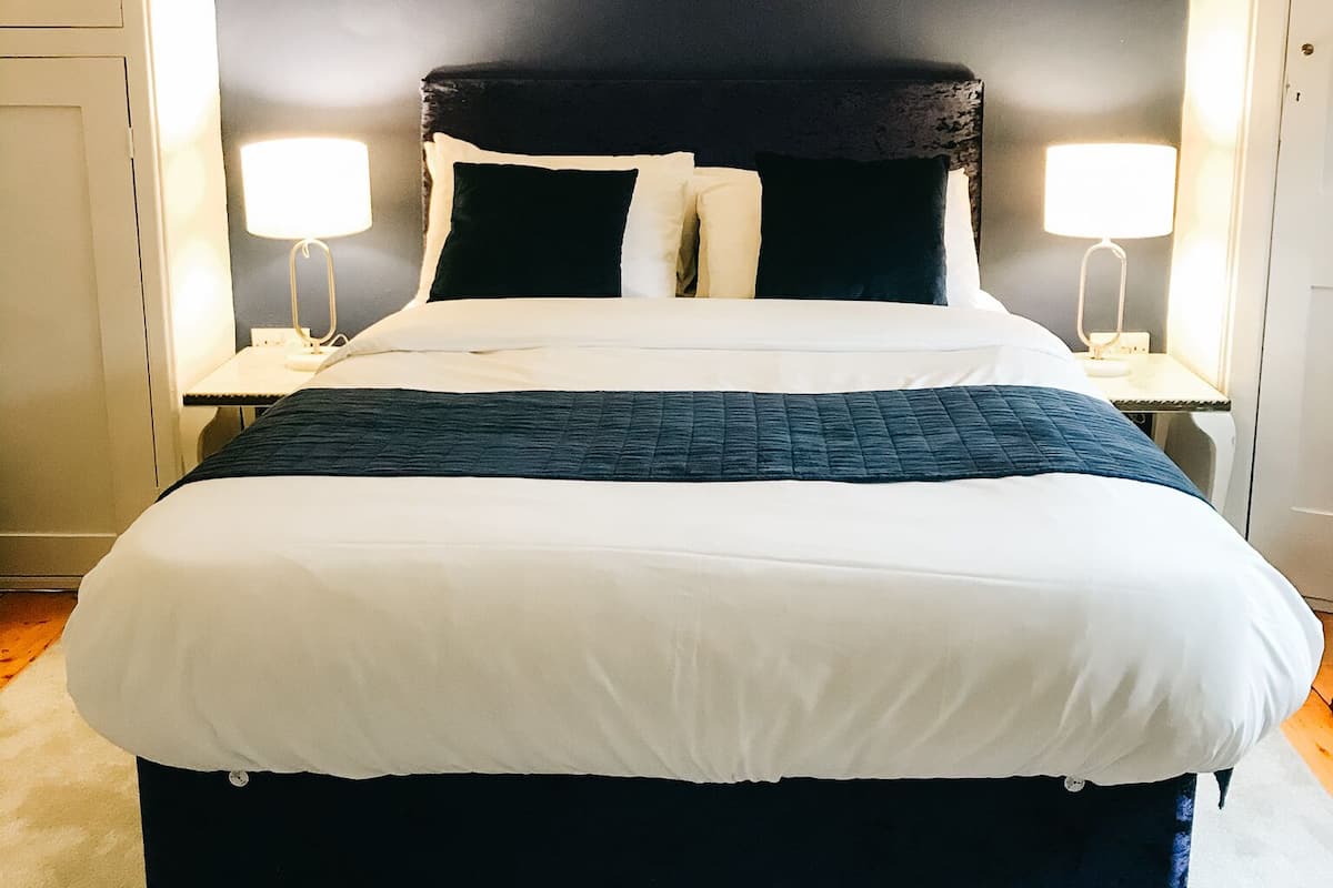 Uma cama grande com cabeceira escura, roupa de cama branca e duas luminárias de cabeceira.