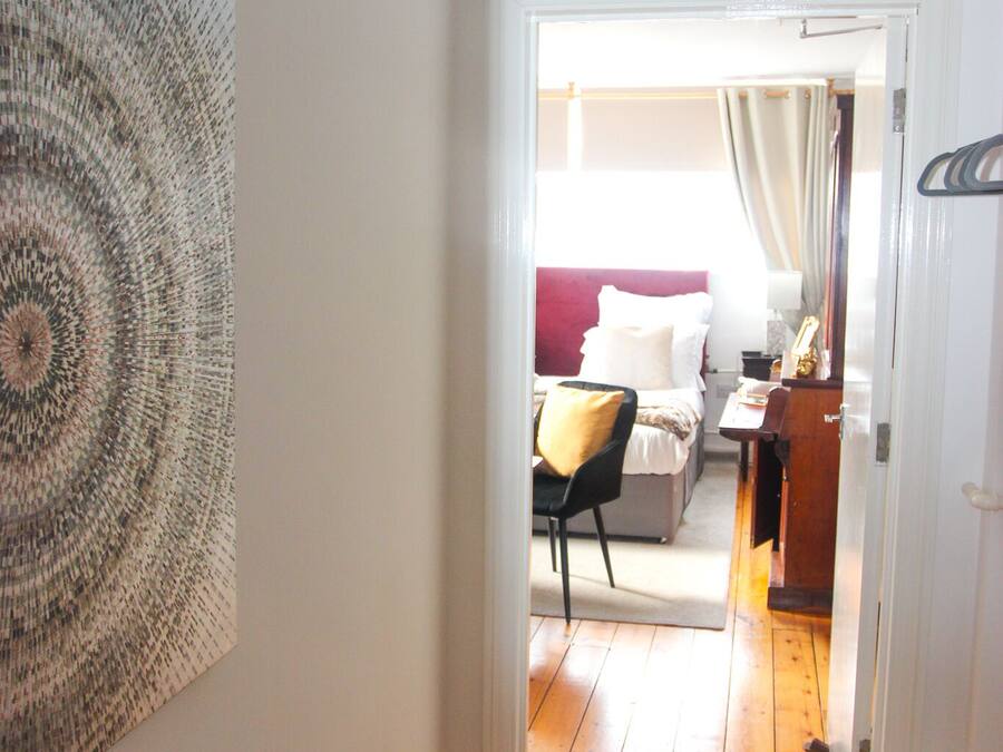 Corredor que dá para um quarto com uma cama, uma cadeira e uma mesa de cabeceira.