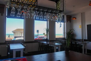 Restaurante com vista para a praia, janelas amplas e taças de vinho penduradas.
