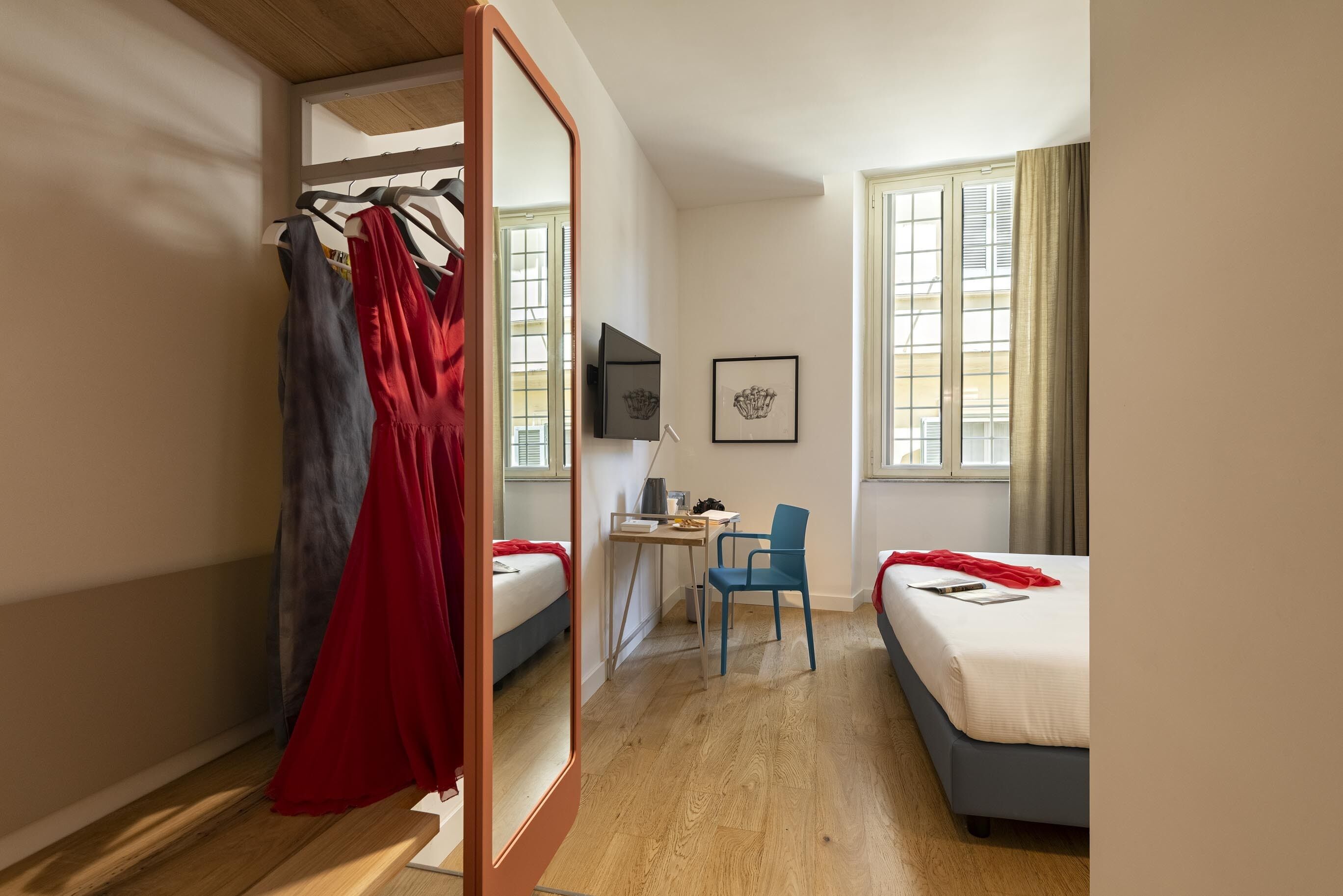 Quarto de hotel com duas camas, uma escrivaninha, uma cadeira, uma televisão e um guarda-roupa.