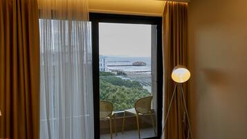 Quarto de hotel com uma janela grande, uma luminária de chão e duas cadeiras.