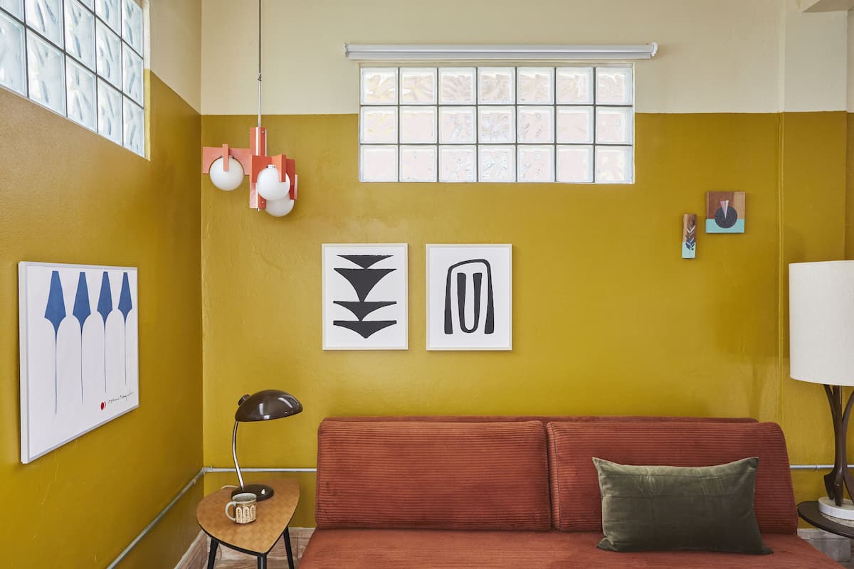 Quarto com parede amarela, sofá vermelho e obra de arte na parede.