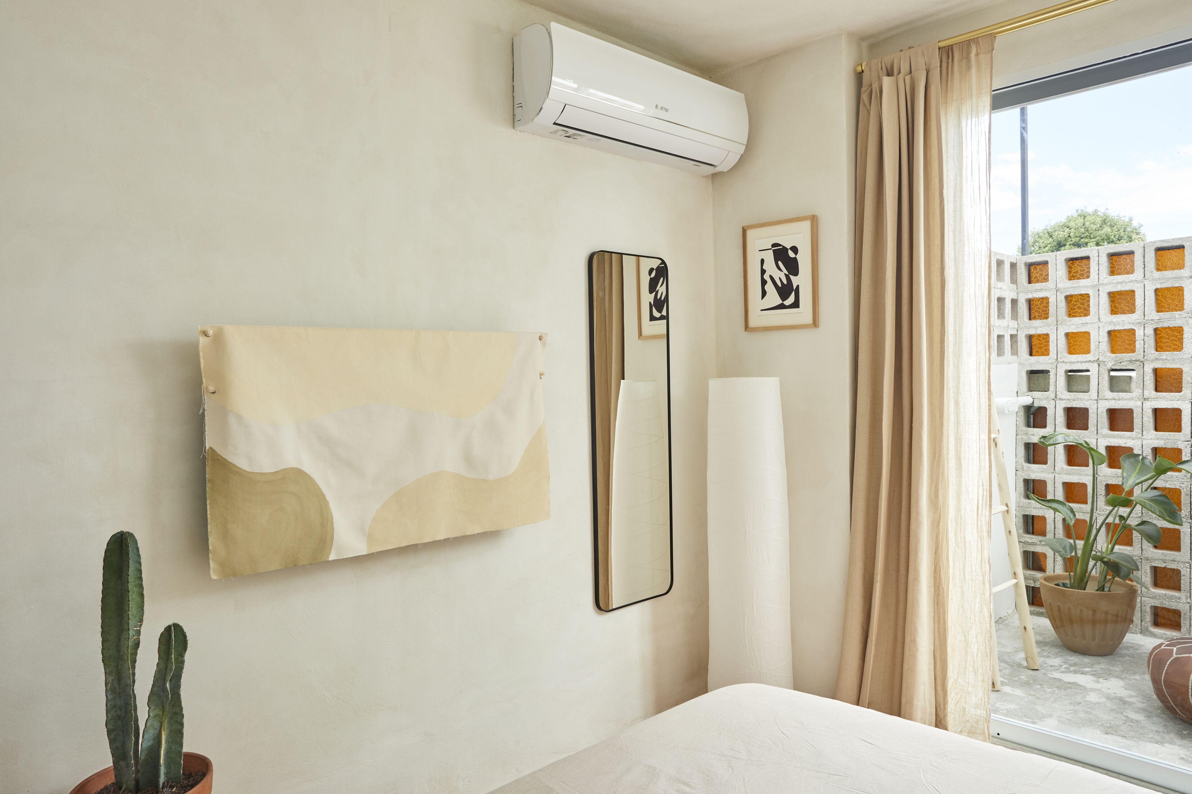 Quarto com cama, ar condicionado na parede, espelho, quadro e janela com cortinas.