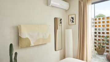 Quarto com cama, ar condicionado na parede, espelho, quadro e janela com cortinas.