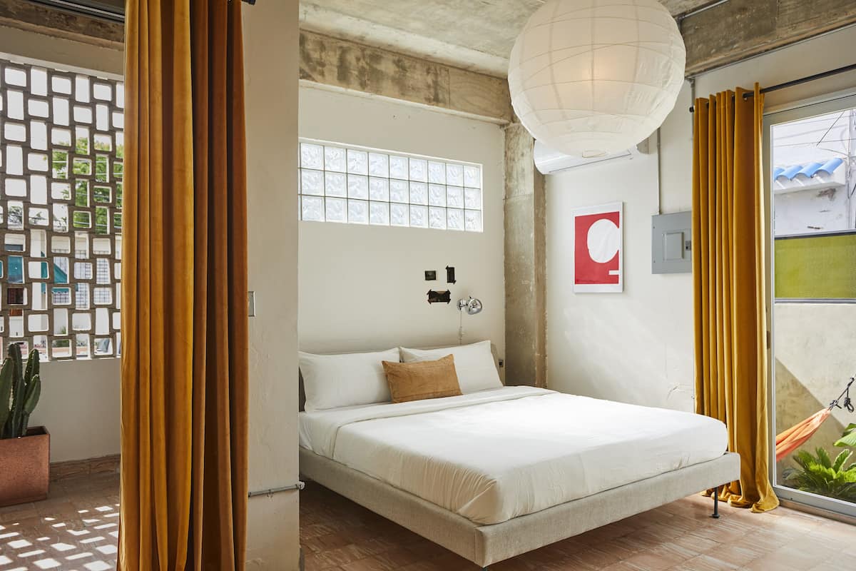Quarto com cama, janela, luminária na parede e cortinas.