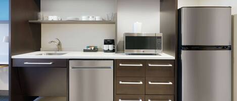Uma cozinha moderna com frigorífico de aço inoxidável, micro-ondas e máquina de lavar louça.
