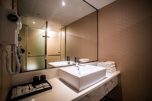 Casa de banho de hotel com um espelho grande, duas bacias, um secador de cabelo e toalhas bem dobradas no balcão.