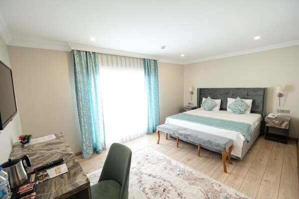 Quarto de hotel com cama, mesas de cabeceira, escrivaninha com cadeira, televisão e cortinas.