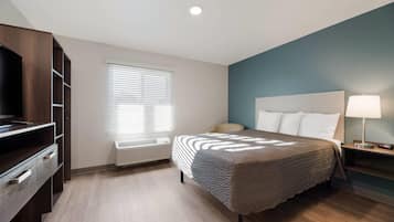 Quarto de hotel com cama, mesa de cabeceira, luminária e televisão sobre um suporte.