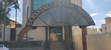 Entrada do Crystal Plaza Hotel, com uma grande placa em arco e uma escadaria que leva à entrada.