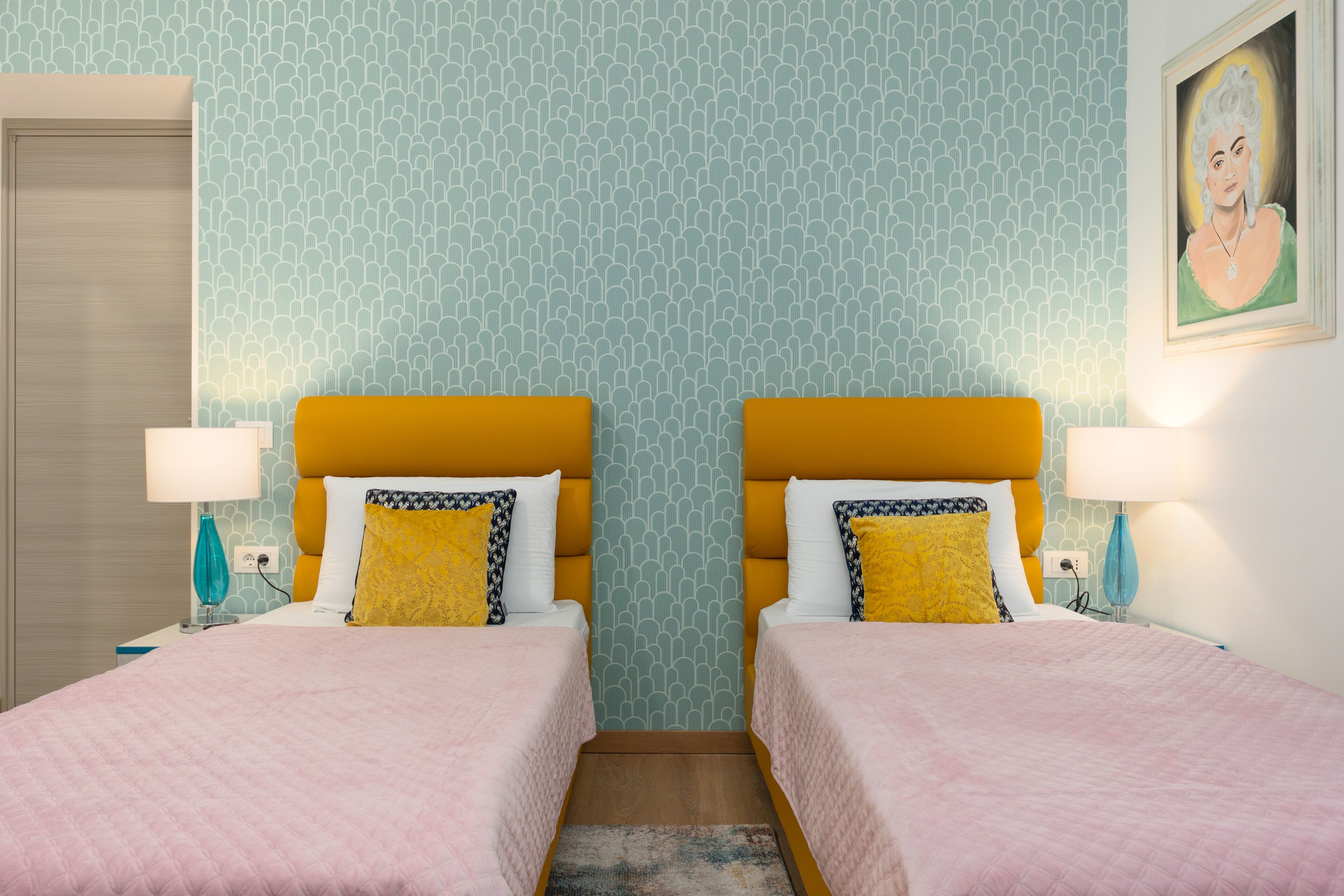 Quarto de hotel com duas camas, parede estampada e um retrato emoldurado.