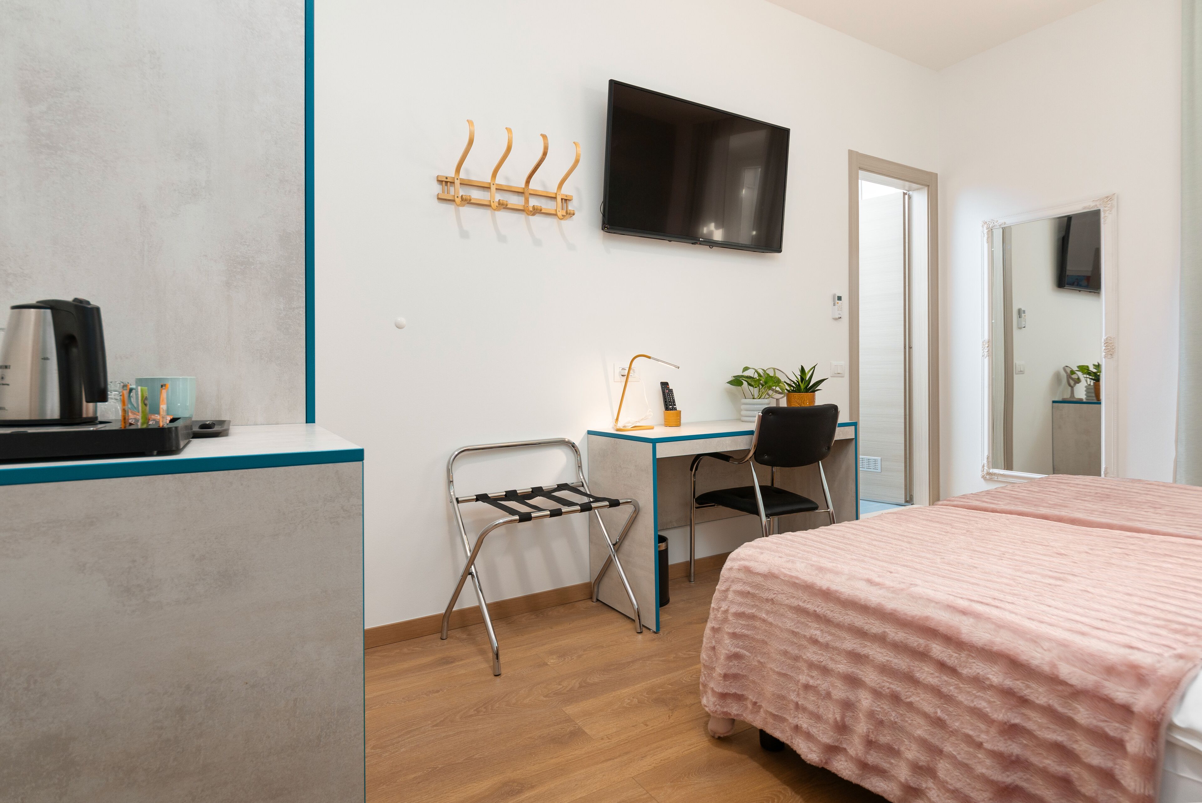 Quarto de hotel moderno com escrivaninha, cadeira, televisão e uma cama com cobertor rosa.