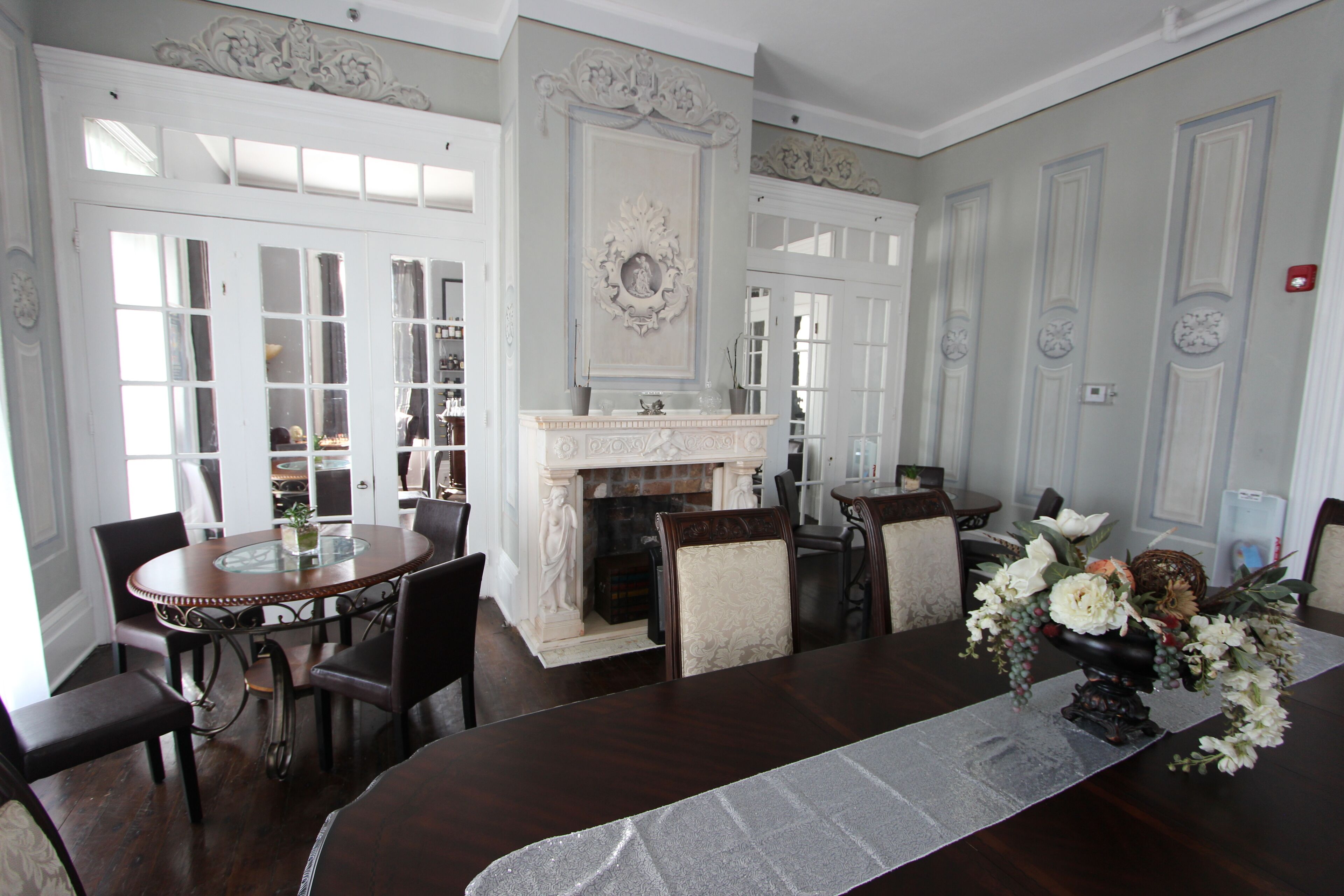 Uma sala de jantar com uma mesa comprida, cadeiras, lareira e um vaso decorativo com flores.