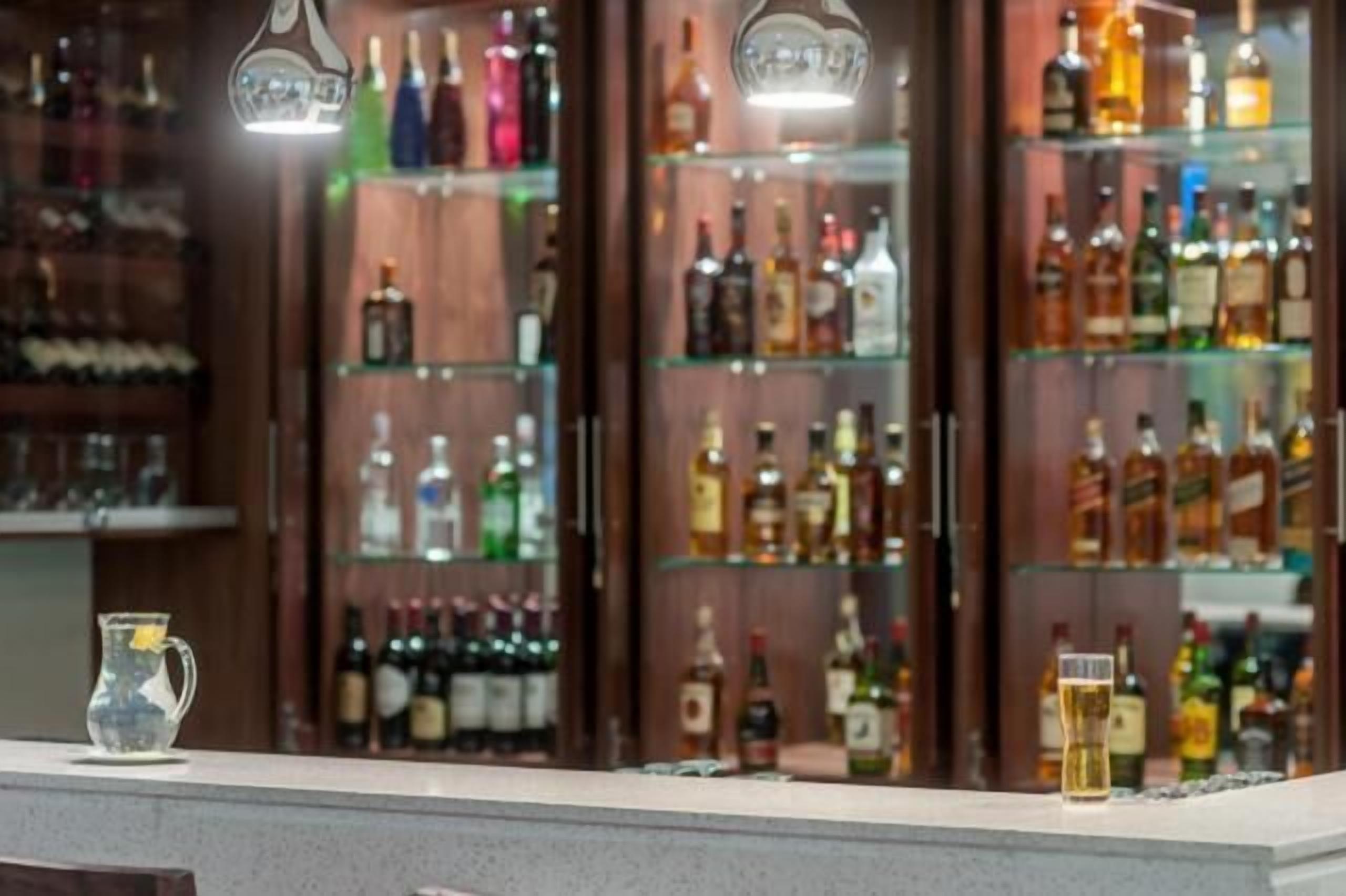 Uma área de bar com prateleiras cheias de garrafas de bebidas e alguns copos no balcão.