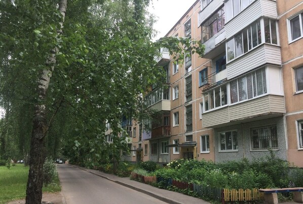 Um edifício residencial com vários andares, varandas, entrada pavimentada e vegetação exuberante.