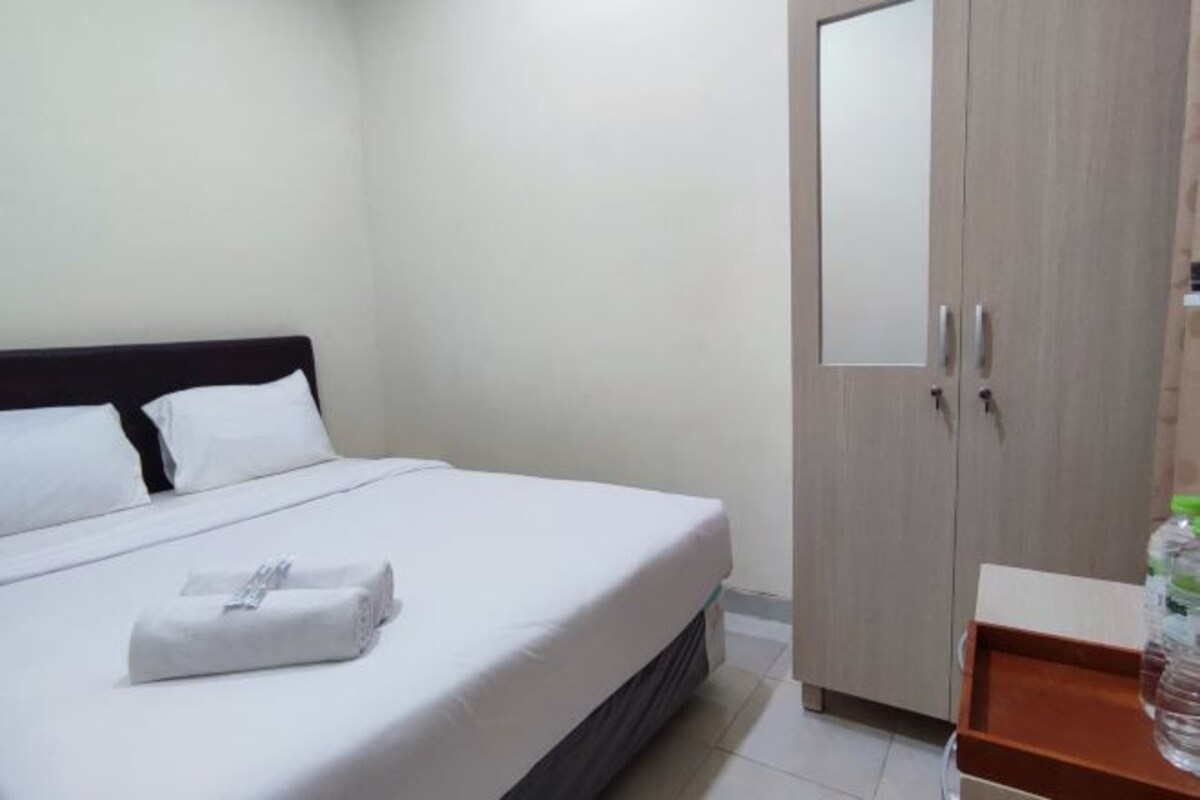 Quarto de hotel com cama, guarda-roupa e uma pequena mesa com uma garrafa.