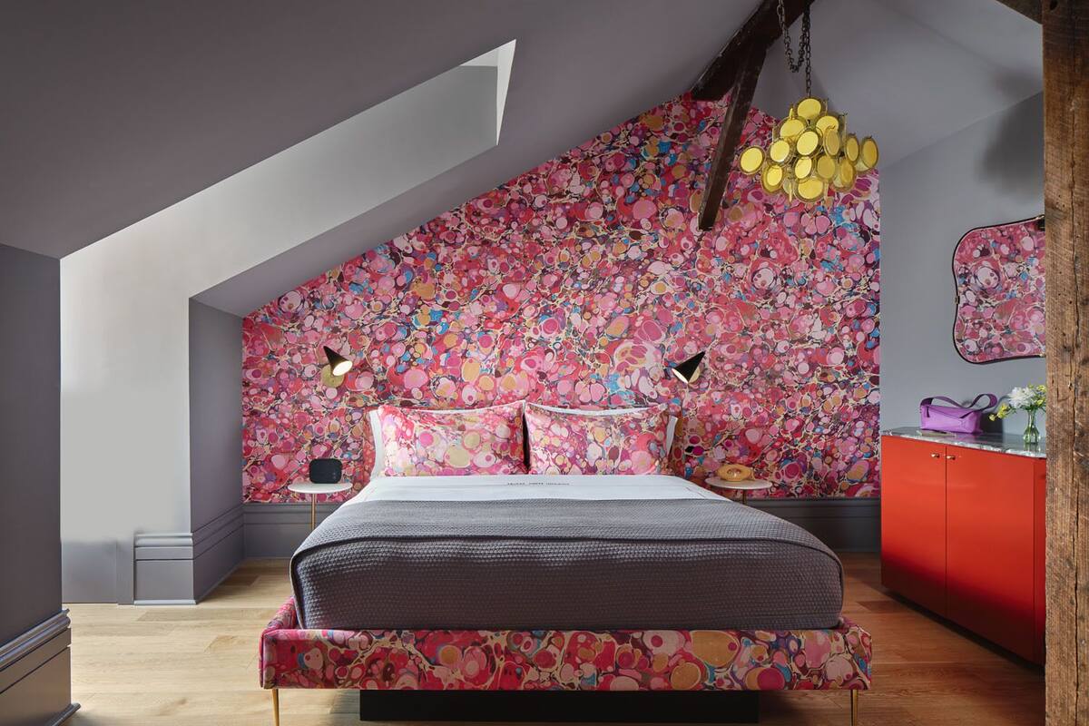 Quarto com teto inclinado, cama com cabeceira estampada com flores, cômoda vermelha e luminária pendente.