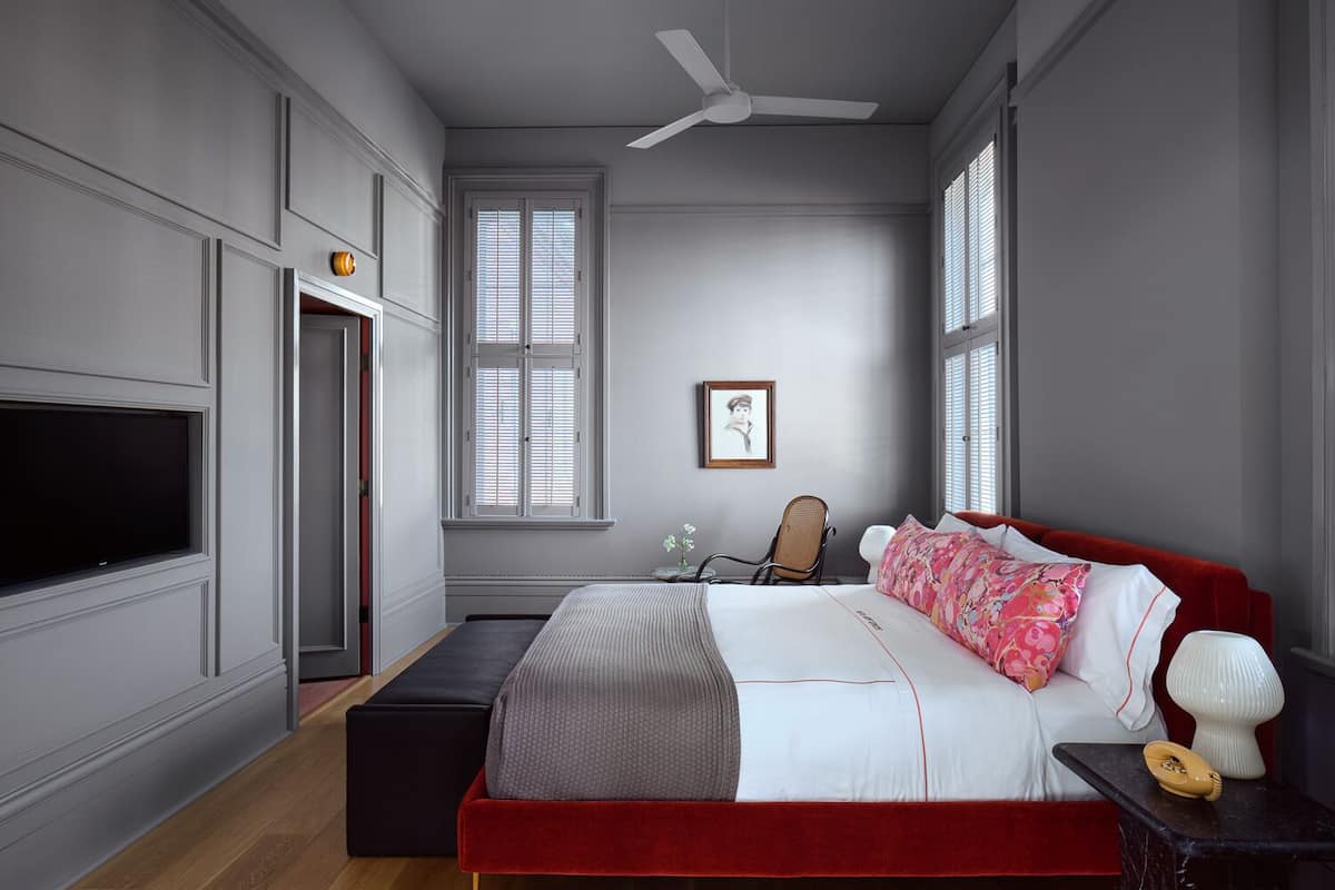 Quarto moderno com uma cama grande, televisão, ventilador de teto e janela com persianas.
